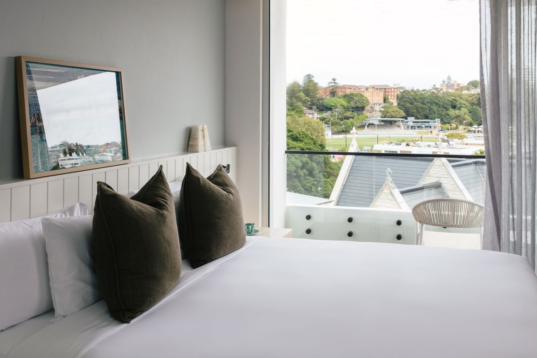 Quarto de hotel com uma cama grande, vista para a paisagem urbana e uma janela com cortinas.
