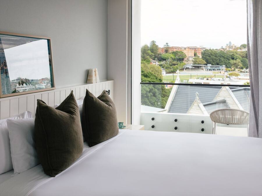 Quarto de hotel com uma cama grande, vista para a paisagem urbana e uma janela com cortinas.