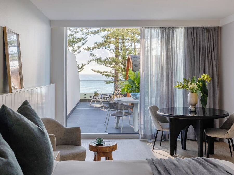 Quarto de hotel com varanda, mesa de jantar e sofá.