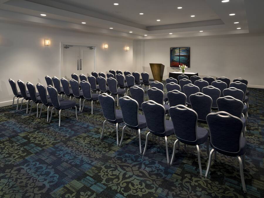 Uma sala de conferências com fileiras de cadeiras, um púlpito e piso coberto de carpete.