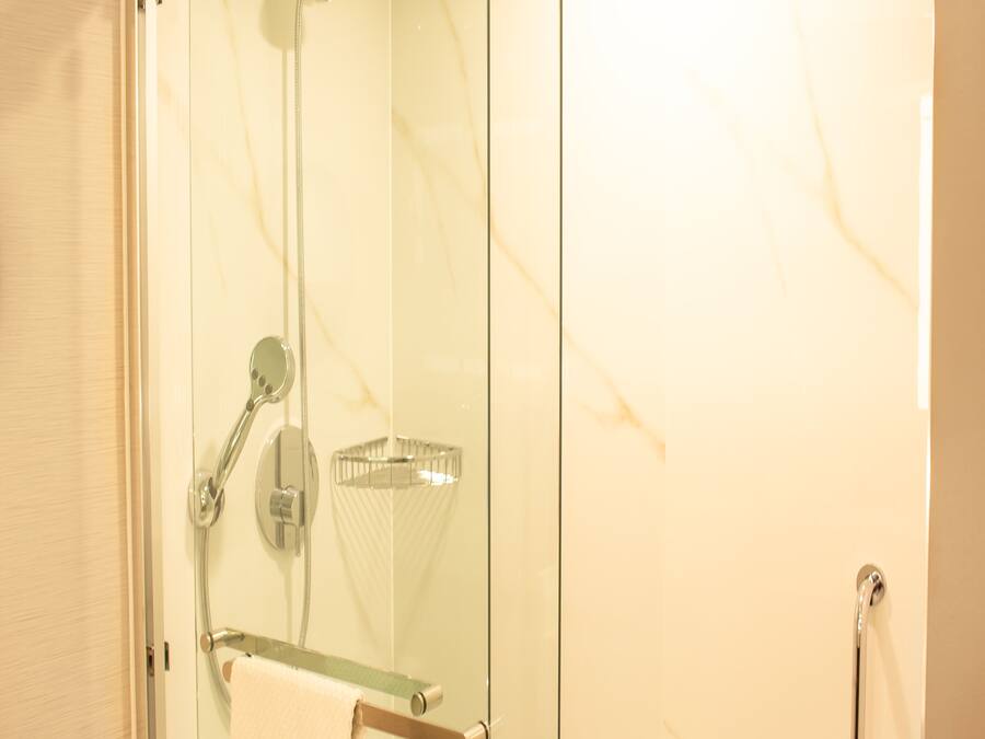 Um chuveiro com divisória de vidro, um chuveiro manual, uma prateleira de vidro e um porta-toalhas.