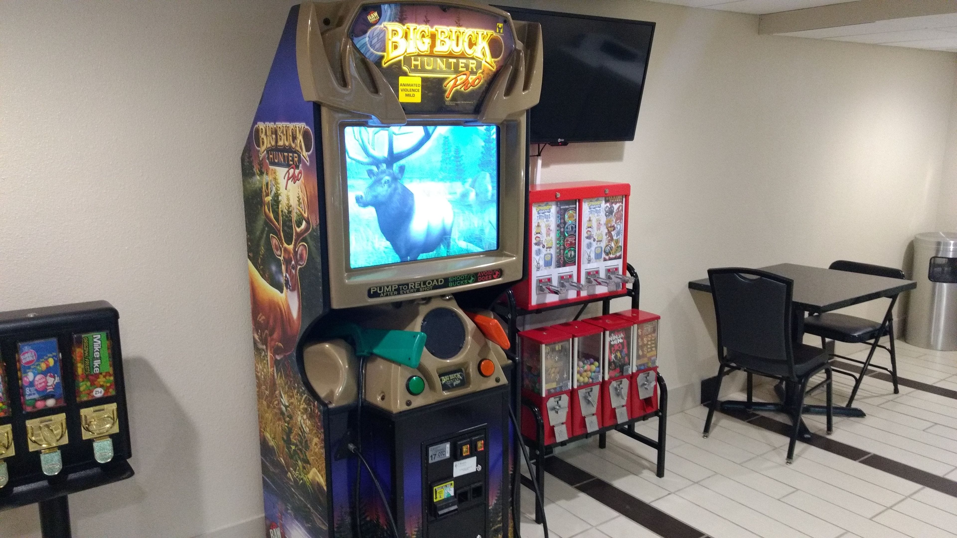 Máquina de jogo Big Buck Hunter Pro com tela de televisão acoplada, rodeada por diversos jogos de arcade e uma lata de lixo.