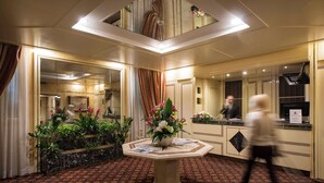 Um saguão de hotel com uma mesa central, plantas em vasos e um carpete estampado.