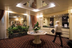 Um saguão de hotel com uma mesa central, plantas em vasos e um carpete estampado.