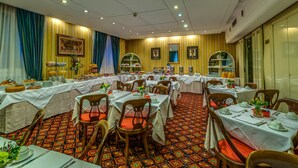 Uma sala de banquetes com várias mesas redondas, cada uma com toalhas brancas, cadeiras e centros de mesa.