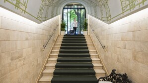 Uma escadaria imponente com alguém subindo, que leva a uma porta com um desenho floral verde.