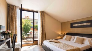 Quarto de hotel com uma cama grande, uma escrivaninha com cadeira, televisão e vista para o exterior.