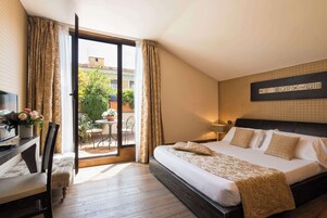Quarto de hotel com uma cama grande, uma escrivaninha com cadeira, televisão e vista para o exterior.