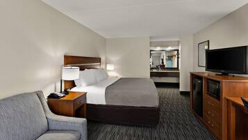 Quarto de hotel com cama, escrivaninha com luminária, televisão e área de estar.