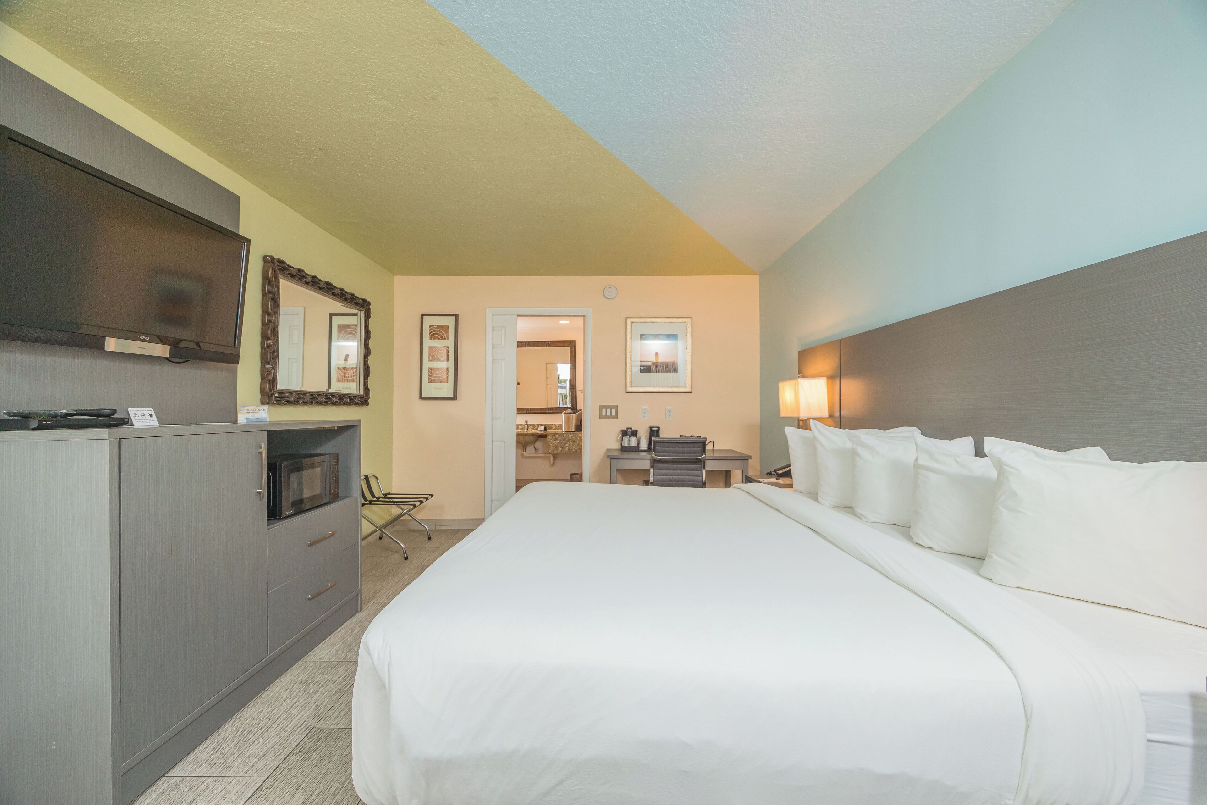 Quarto de hotel com uma cama grande, uma escrivaninha, micro-ondas e televisão.