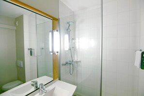Casa de banho com chuveiro de cabine de vidro, lavatório branco e sanita.