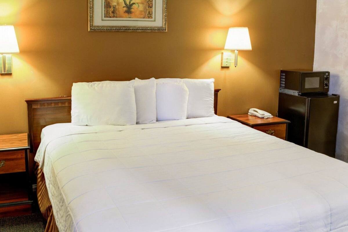 Quarto de hotel com uma cama grande, duas mesas de cabeceira, um criado-mudo, luminária, telefone e geladeira.
