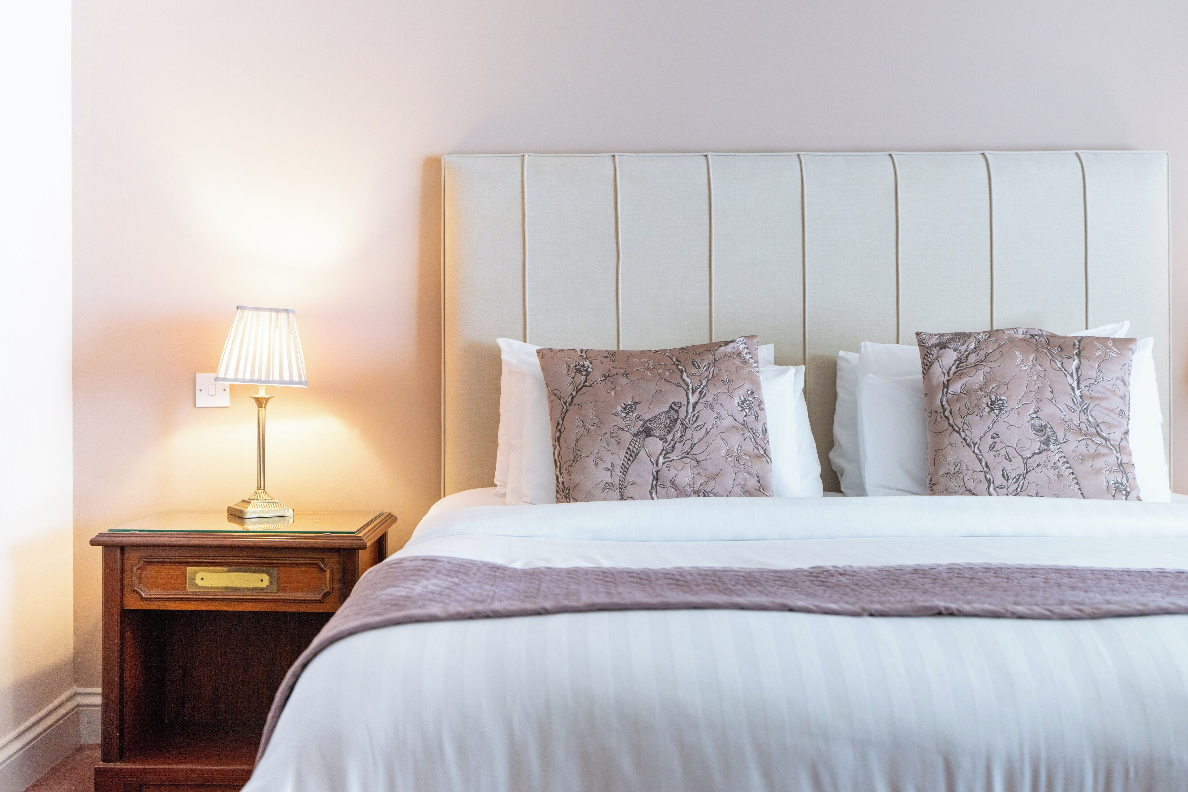 Cama bem arrumada com cabeceira, abajur e duas almofadas decorativas.
