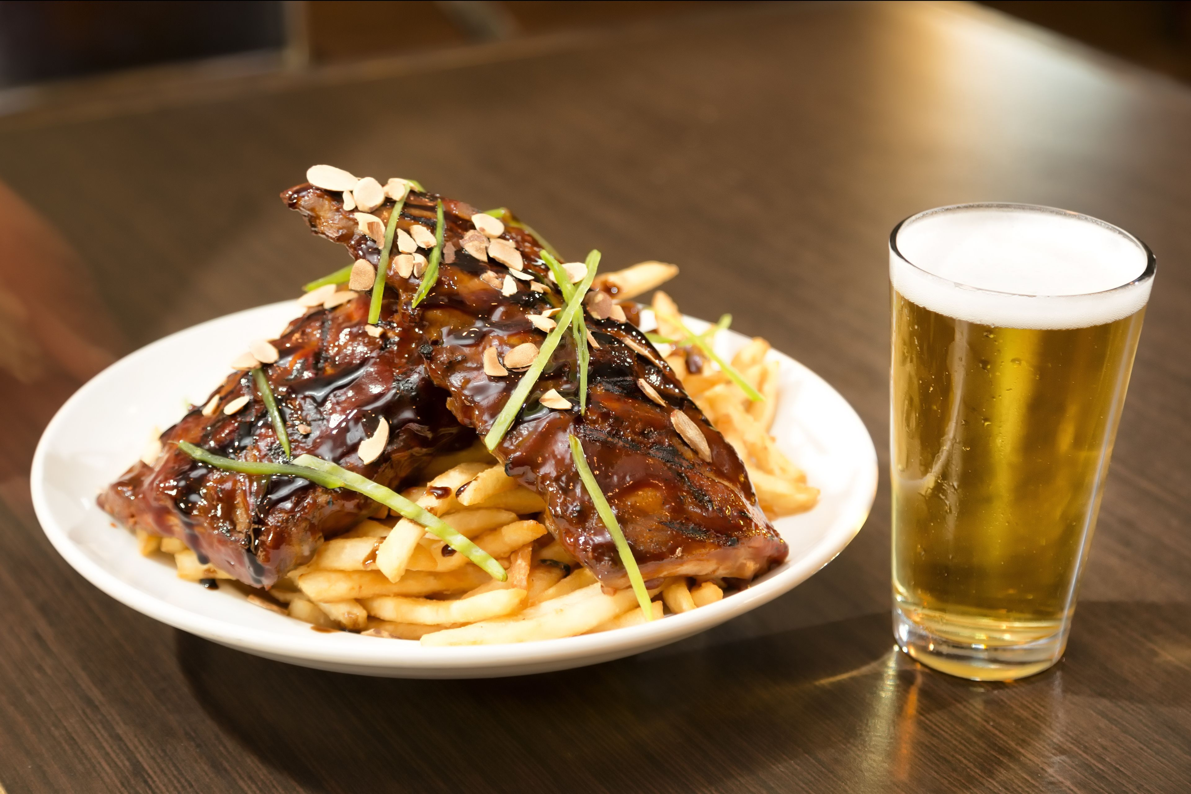 Um prato de costelas com batatas fritas e um copo de cerveja sobre uma mesa de madeira.