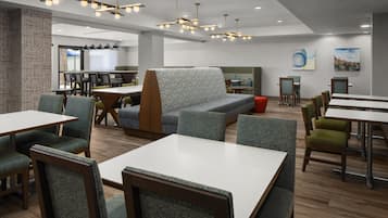 Um lobby de hotel moderno com diversas opções de assento, incluindo um sofá e cadeiras, e uma área de refeições com mesas e cadeiras.