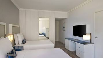 Quarto de hotel com duas camas, uma escrivaninha, uma televisão de tela plana, um abajur e um espelho.