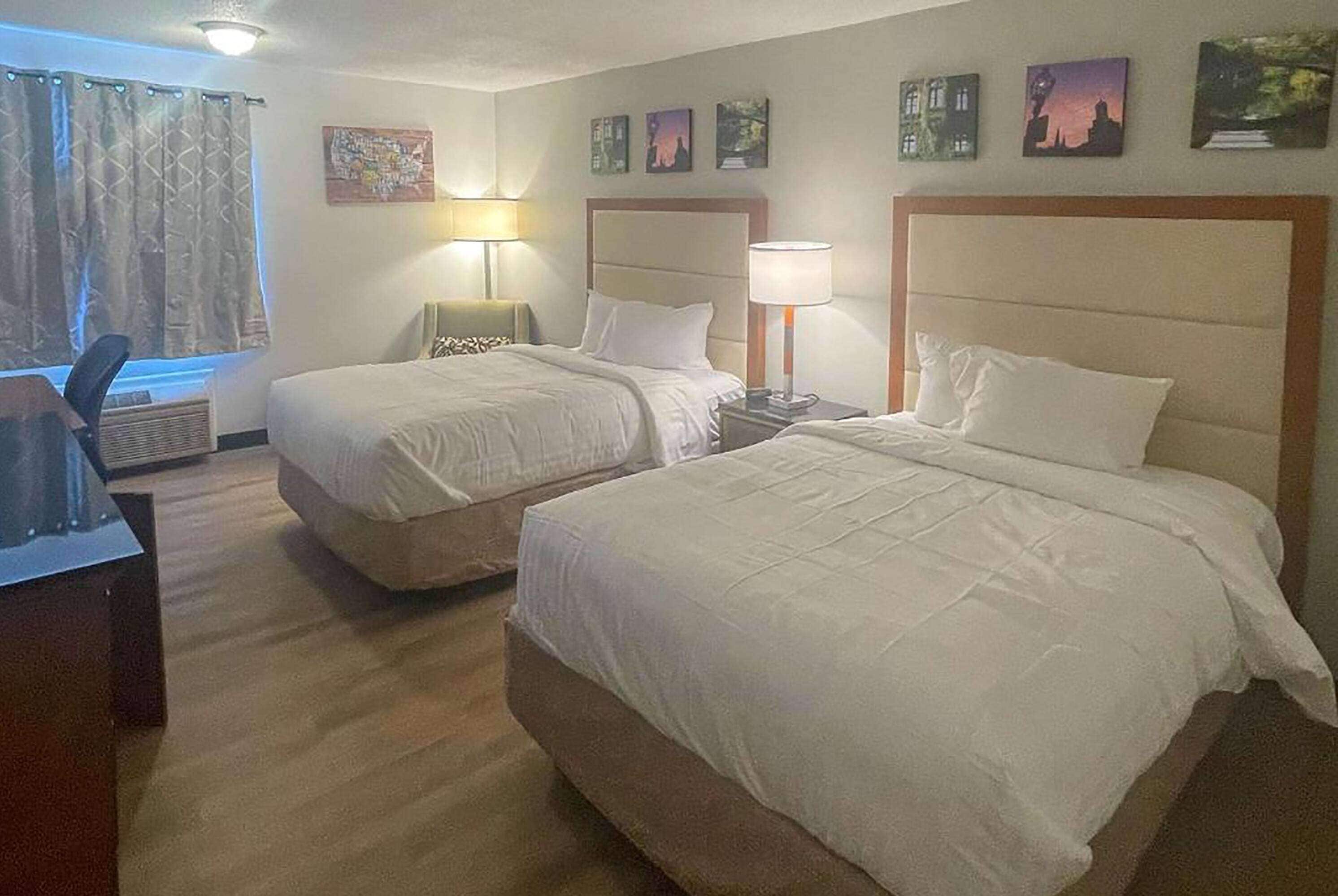 Quarto de hotel com duas camas, uma escrivaninha e uma janela com cortinas.