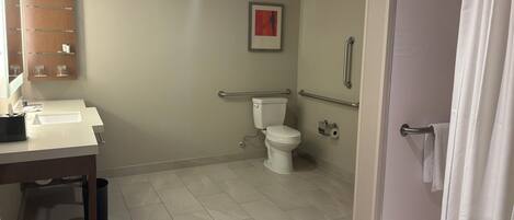 Uma casa de banho moderna com sanita, bidé e secador de mãos. Há uma pia com espelho em cima e um porta-toalhas.