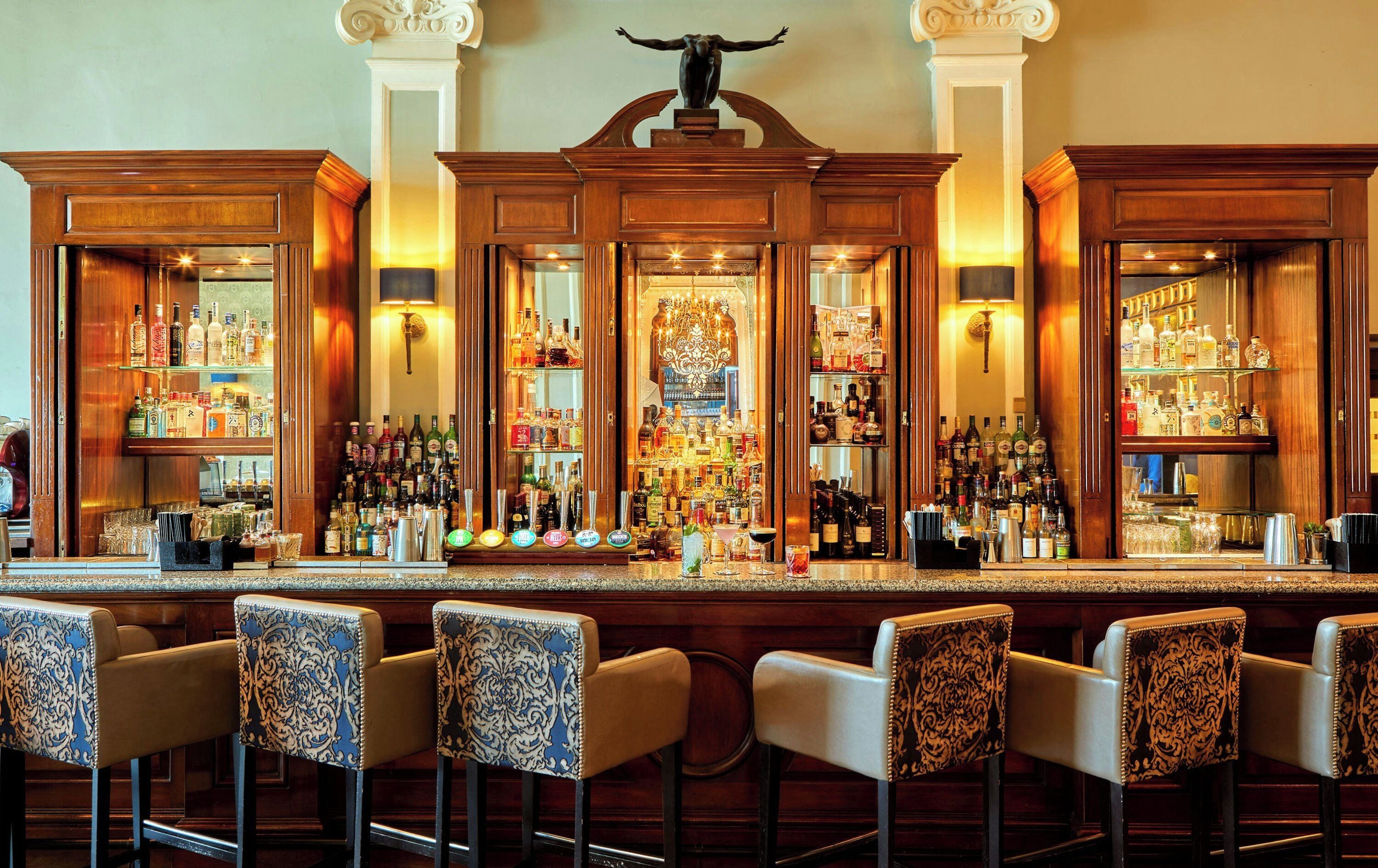 Bar com variedade de garrafas de bebidas, um lustre e banquetas.