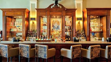 Bar com variedade de garrafas de bebidas, um lustre e banquetas.