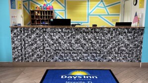 Uma área de recepção com design geométrico na parede, balcão de atendimento e tapete azul com o logotipo Days Inn.