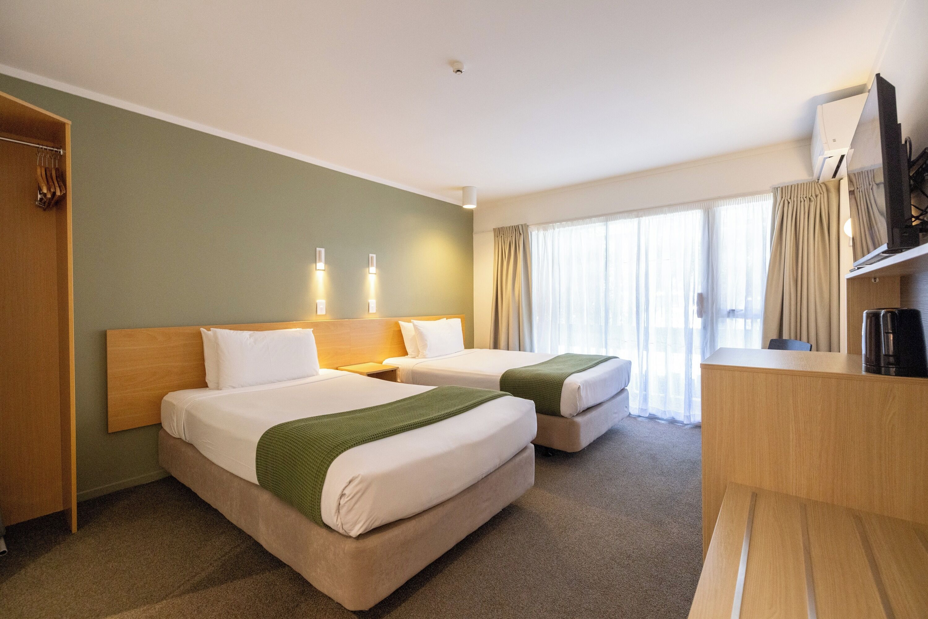 Quarto de hotel com duas camas, uma escrivaninha, televisão e guarda-roupa.