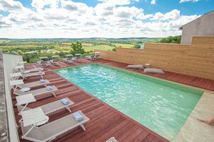 Piscina no terraço com espreguiçadeiras e vista para o campo.