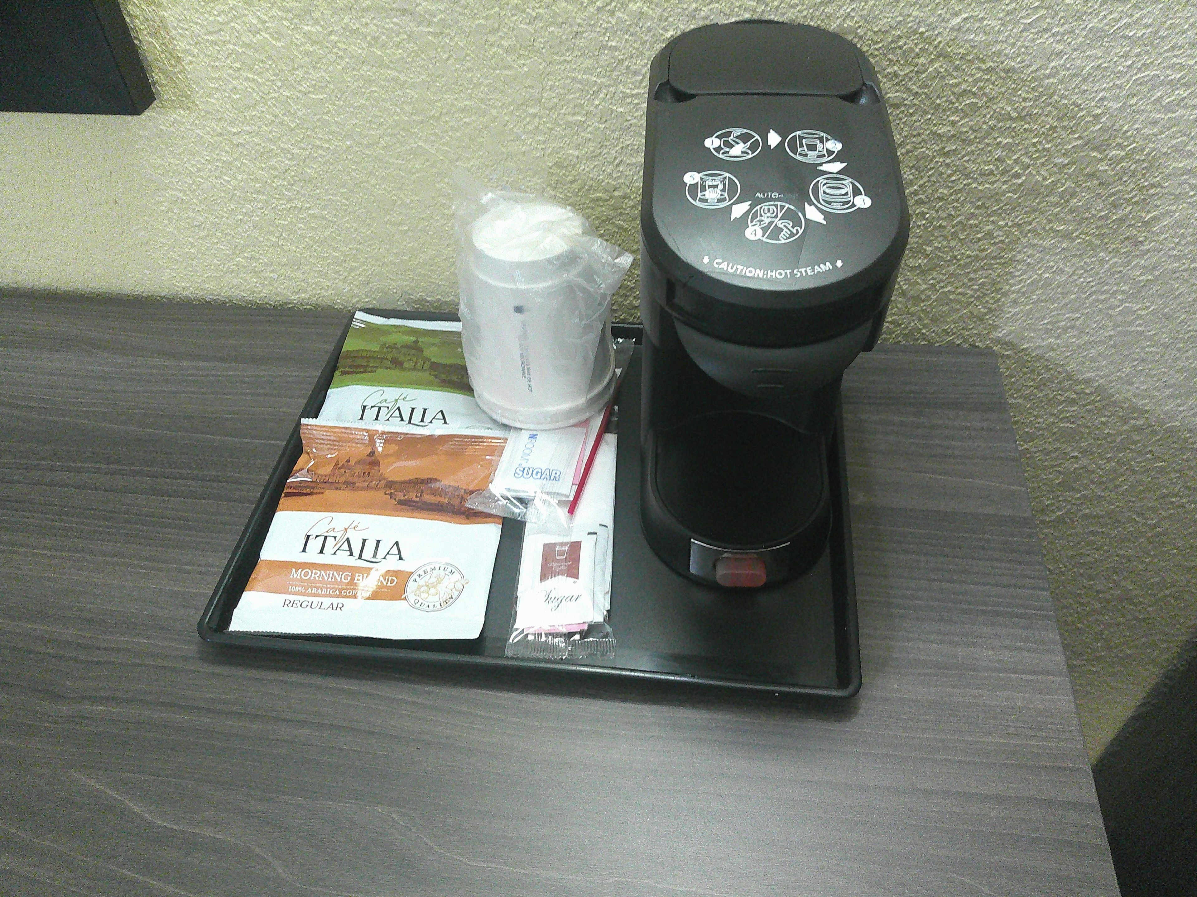 Uma máquina de café sobre uma bandeja, com um pod de café e um copo.