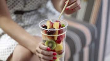 Uma pessoa segurando um copo de plástico transparente cheio de diversas frutas e um canudo.