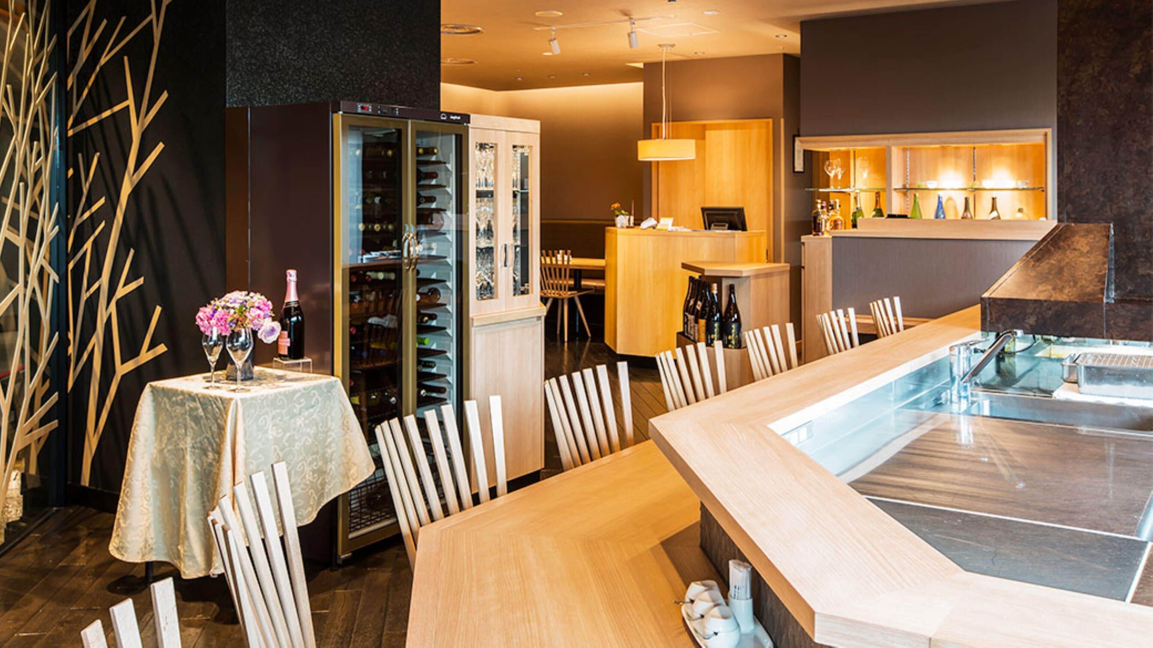 Espaço de refeições moderno em hotel, com uma mesa comprida, cadeiras, um resfriador de vinhos e um bar.