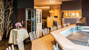 Espaço de refeições moderno em hotel, com uma mesa comprida, cadeiras, um resfriador de vinhos e um bar.