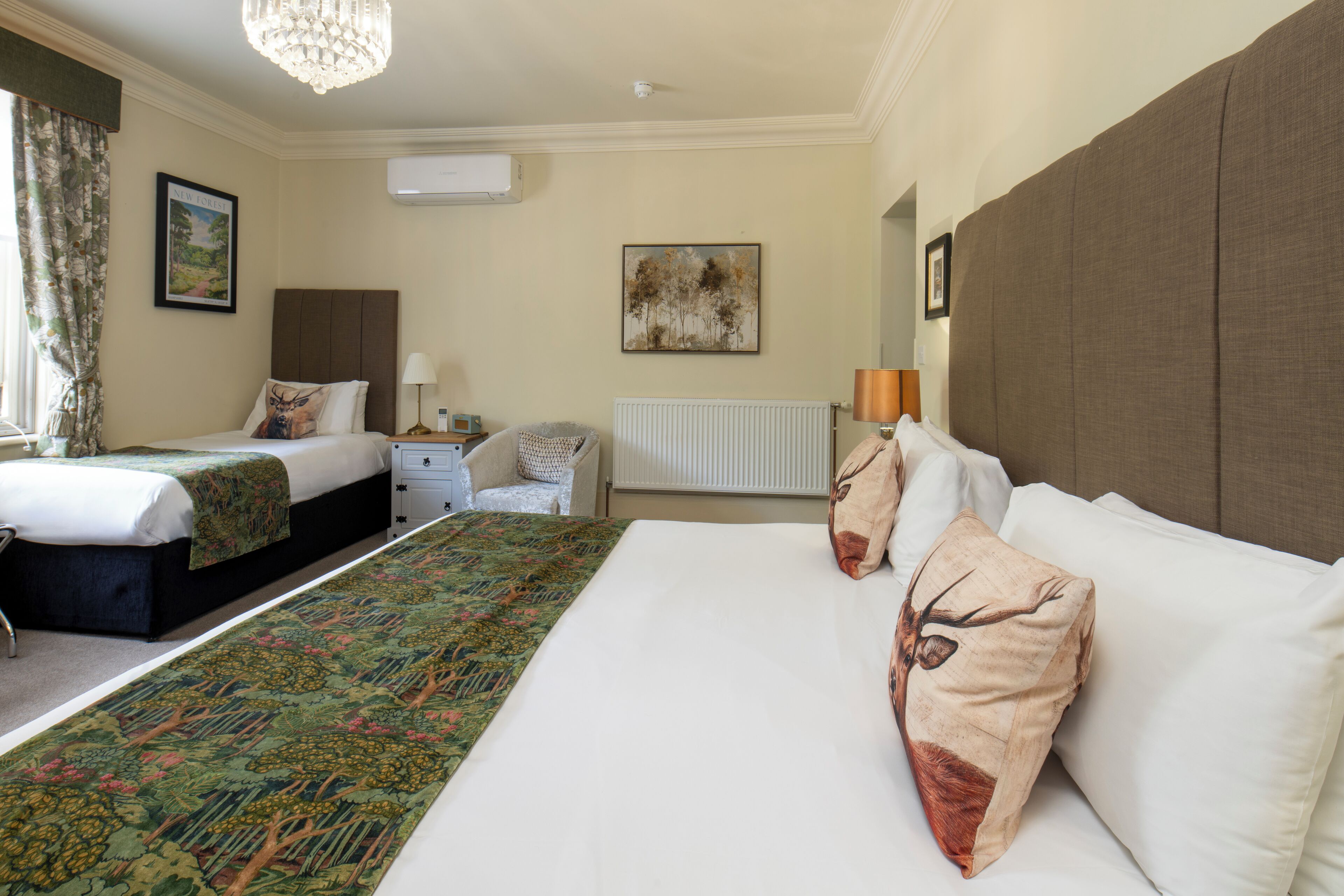 Quarto de hotel com duas camas, uma janela grande com cortinas, um radiador e um quadro na parede.