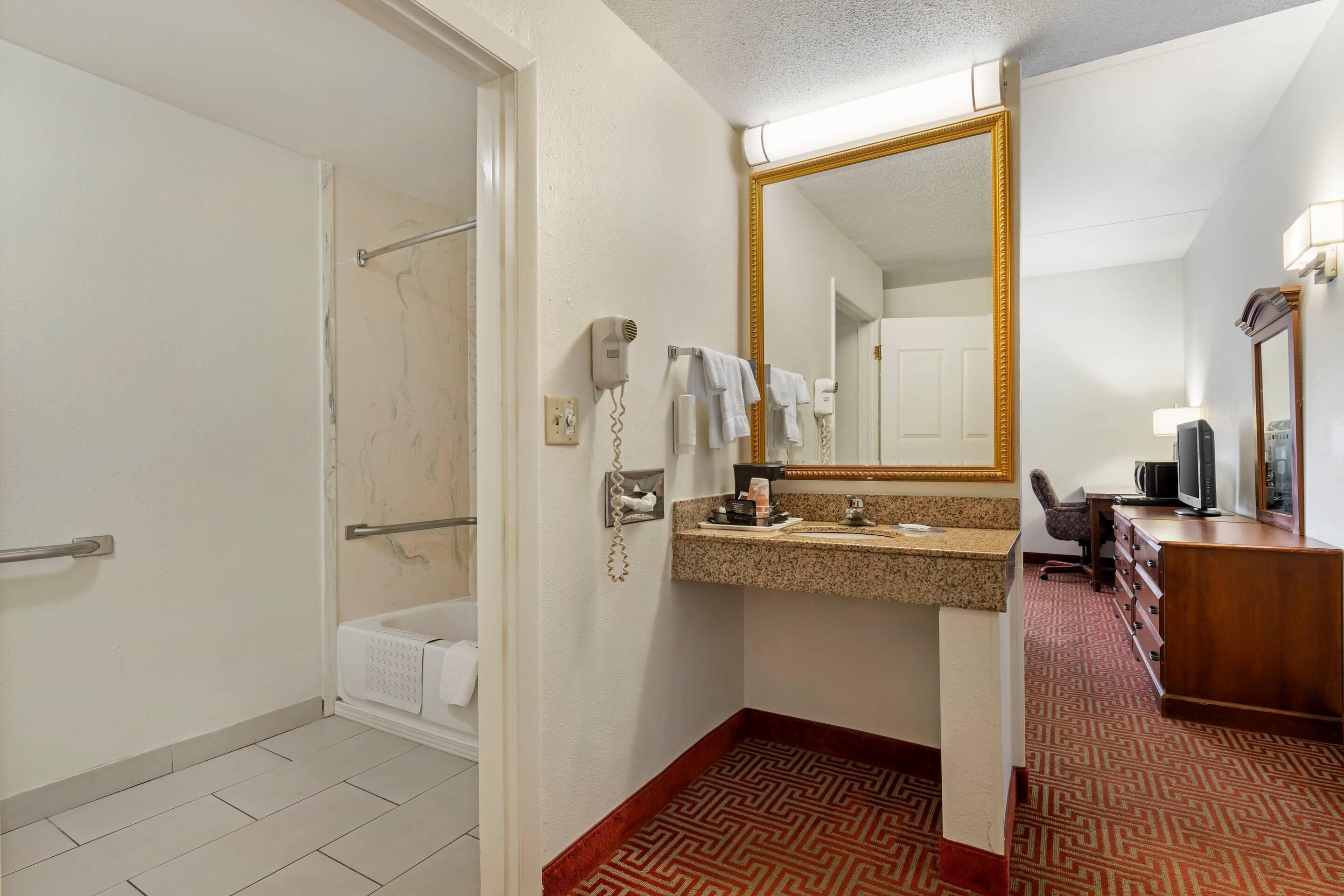 Casa de banho de hotel com chuveiro, lavatório com espelho e secretária com cadeira.