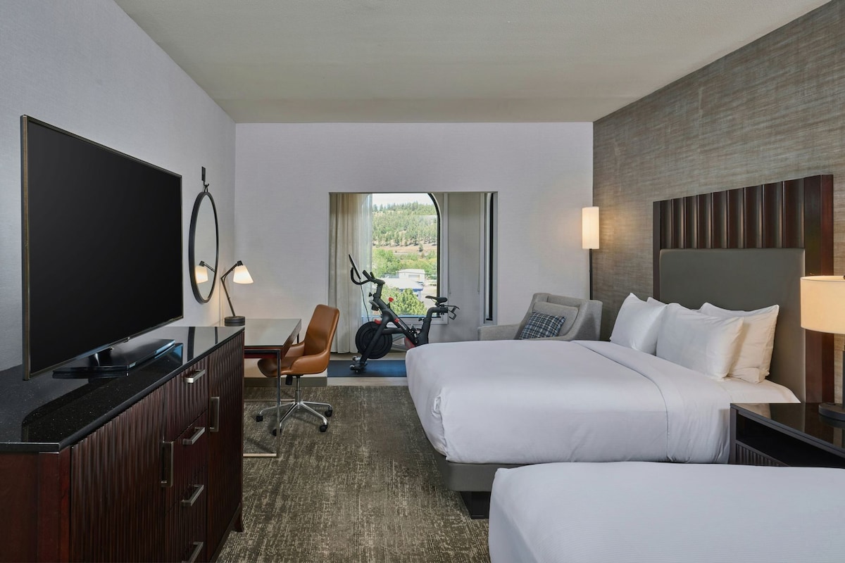 Quarto de hotel com cama, escrivaninha, televisão e vista para o exterior.