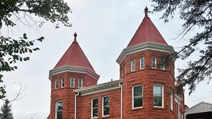 Um edifício de tijolos vermelhos com uma torre central e duas torres menores, uma escadaria que leva à entrada e um gramado bem cuidado.