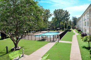 Piscina cercada por uma vedação, com área gramada e um edifício ao fundo.