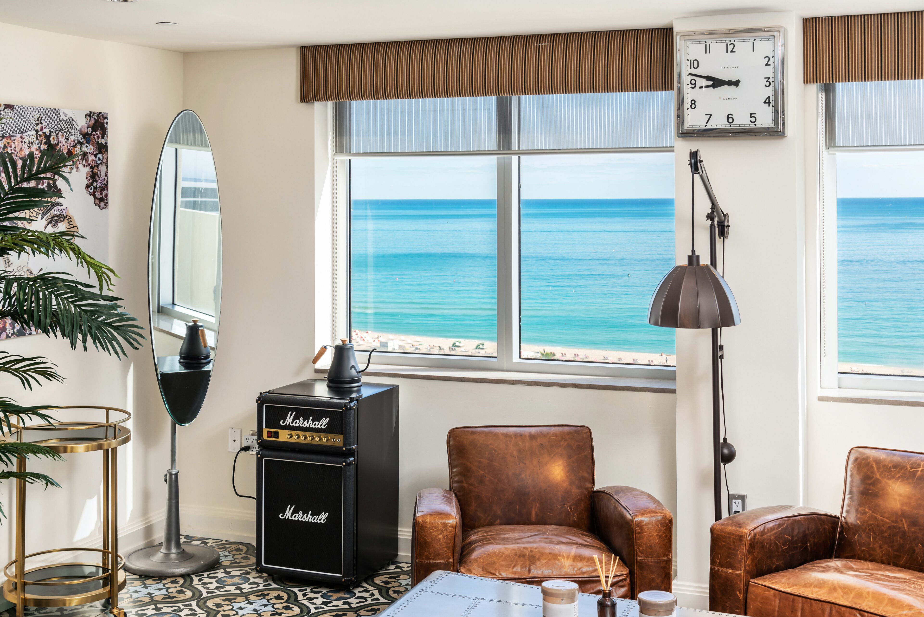 Quarto com vista para o oceano, um relógio, um amplificador Marshall, poltronas de couro e um vaso com planta.