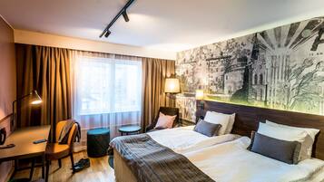 Quarto de hotel com cama, escrivaninha, cadeira, luminária e um grande mural na parede.