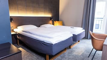 Uma cama de casal com cabeceira, mesas de cabeceira, uma cadeira e uma janela com cortinas.