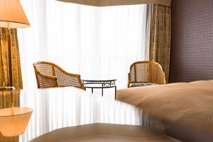 Quarto de hotel com duas cadeiras de vime, uma mesa redonda pequena e uma cama.