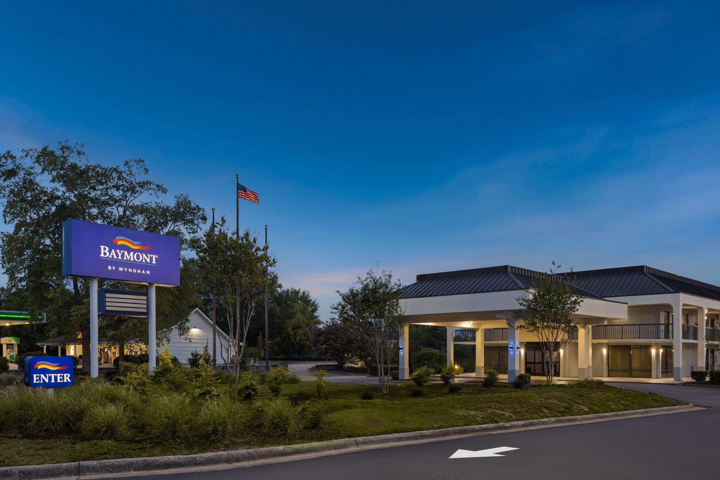 Entrada de hotel com uma bandeira, uma placa e um edifício com galeria coberta.