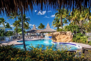 Piscina com rochedo, espreguiçadeiras e palmeiras.