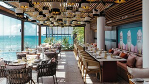 Restaurante com área externa e mesas de frente para o mar, com iluminação moderna e vista do oceano.