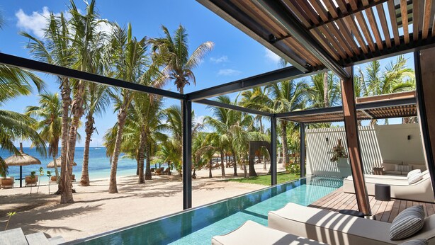 Piscina infinita com paredes de vidro e vista para uma praia e palmeiras.