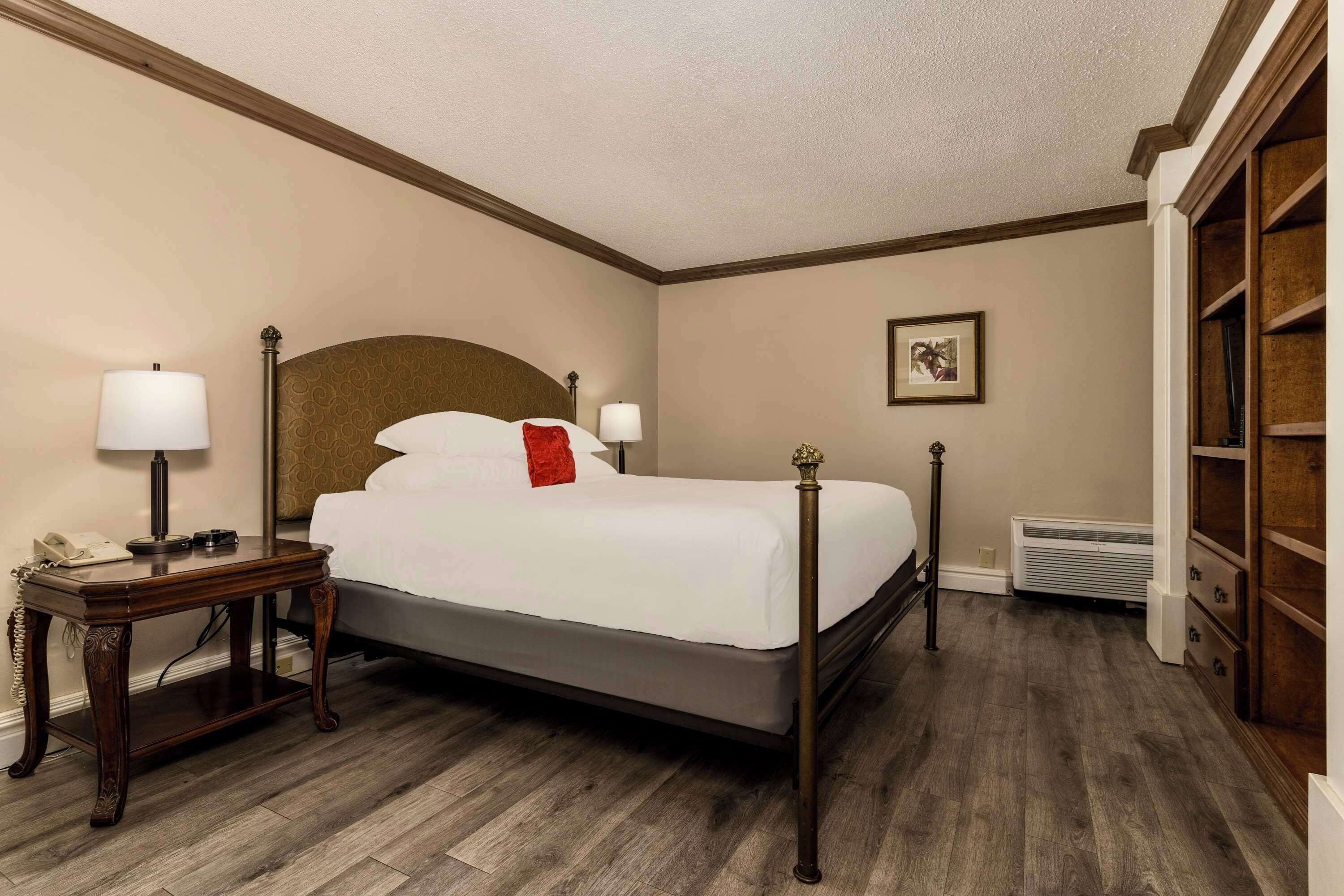 Quarto de hotel com cama, mesas de cabeceira, abajur, quadro emoldurado e armário embutido.