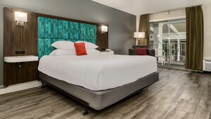 Quarto de hotel com uma cama grande, uma mesa de cabeceira, uma luminária na parede e vista para o exterior através de uma porta de vidro deslizante.