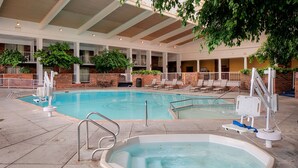 Piscina interior com hidromassagem, espreguiçadeiras e um terraço coberto com paredes de tijolo e vegetação.