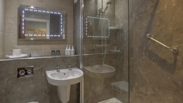 Um banheiro moderno com chuveiro em gabinete de vidro, duas pias, espelho com iluminação LED e vaso sanitário.