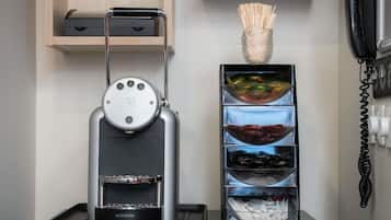 Uma máquina de café Nespresso com reservatório de água, um recipiente de vidro com cabo de madeira e um celular sobre a mesa.