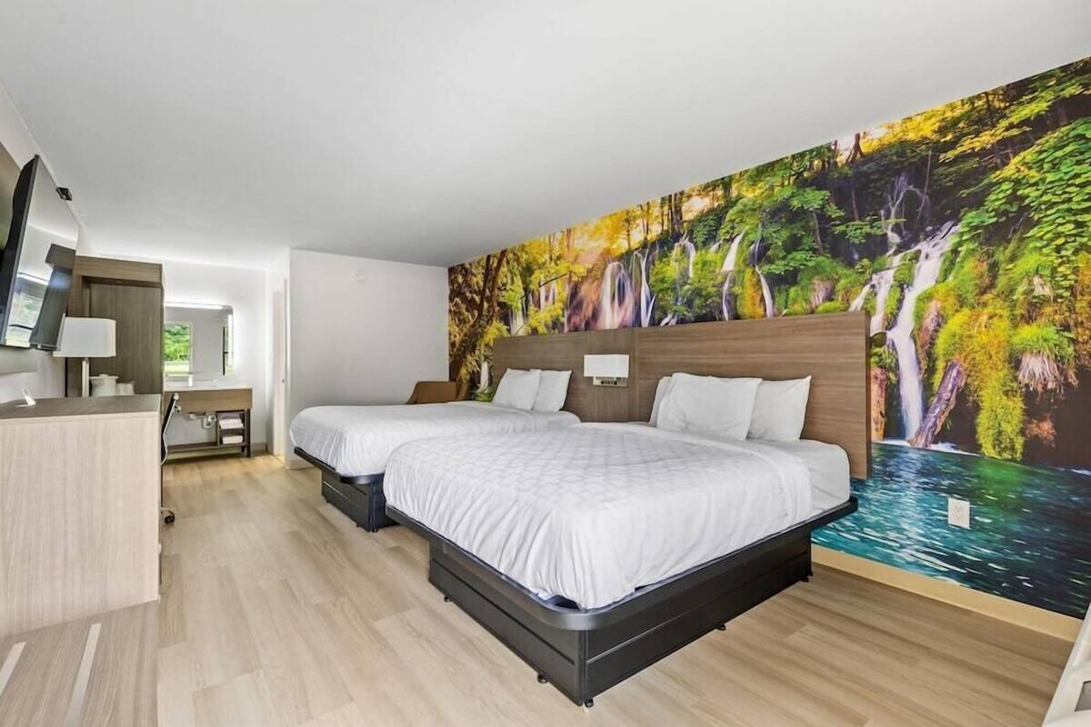 Quarto de hotel com duas camas, uma escrivaninha e um grande mural na parede retratando uma cachoeira.